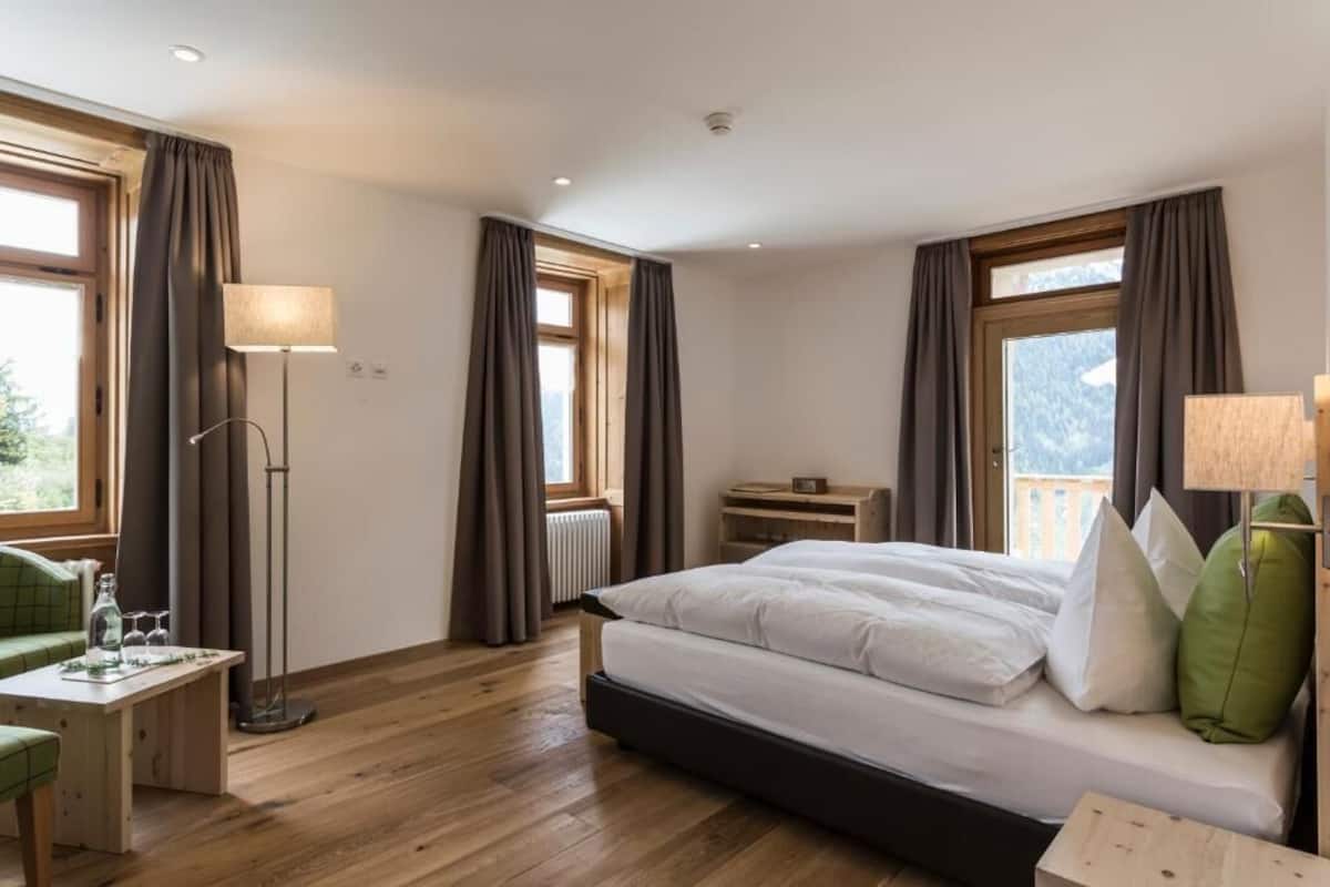Quarto com cama, mesa de cabeceira, abajur e vista para o exterior.