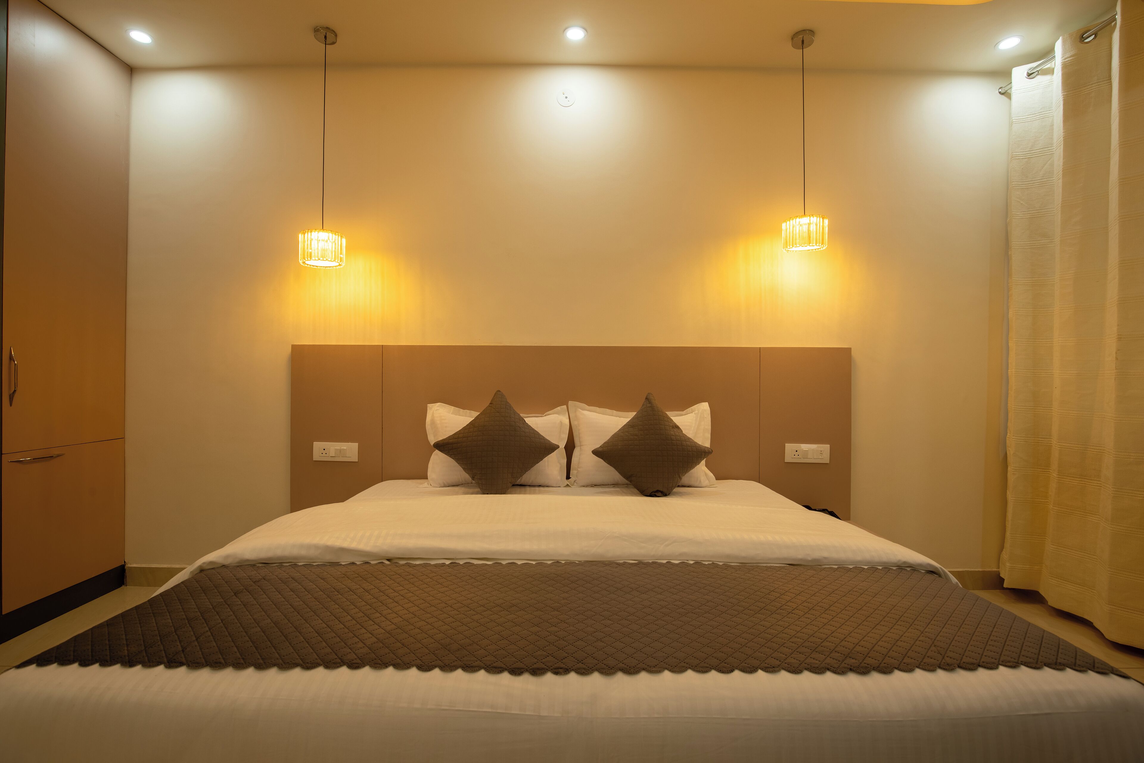Quarto de hotel com uma cama grande, duas luminárias de cabeceira e uma cortina na janela.