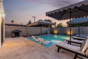 Um quintal com piscina, espreguiçadeiras e churrasqueira.
