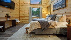 Quarto de cabana de madeira com cama, mesa de cabeceira e janela com cortinas.