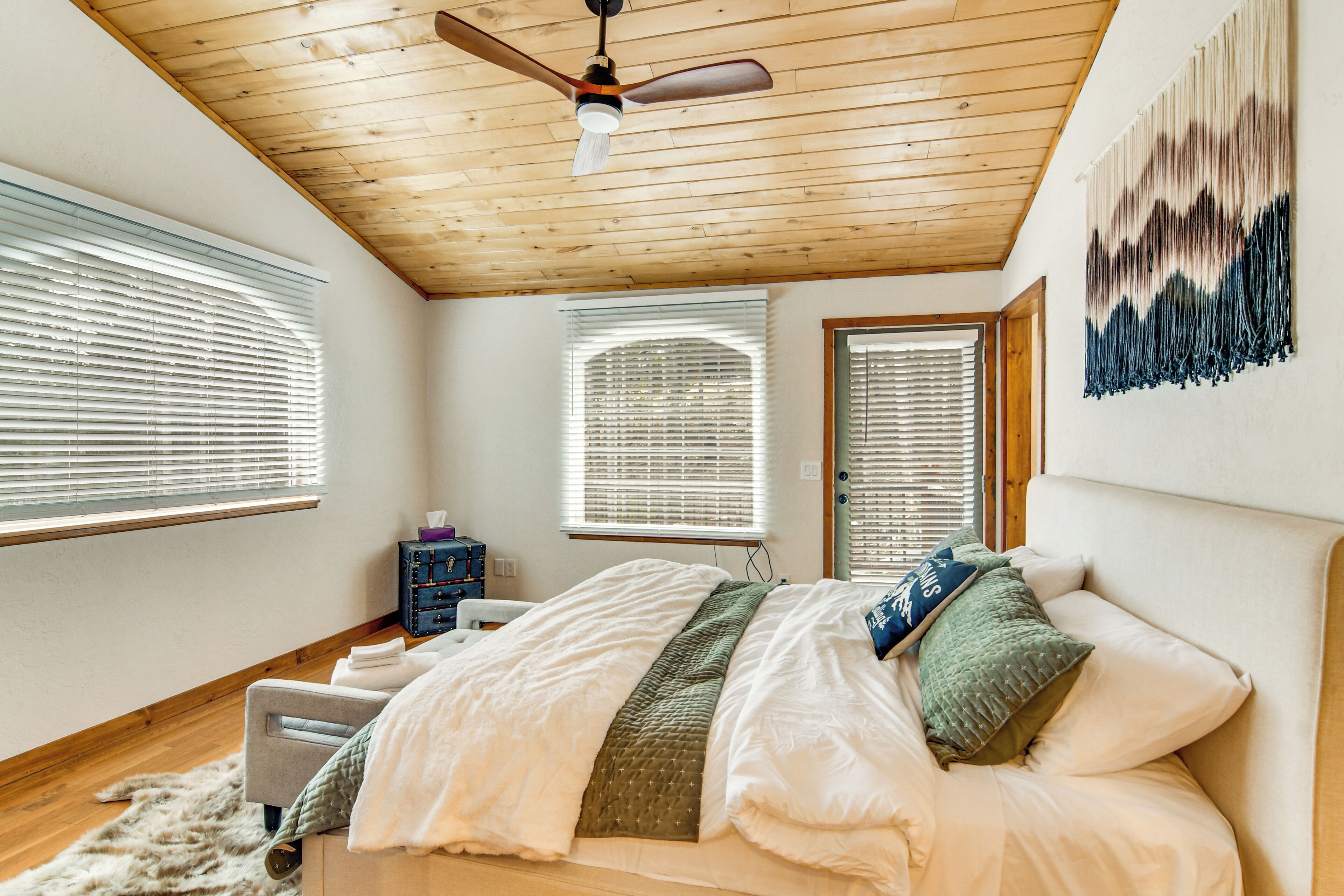 Quarto com teto de madeira, cama com roupa de cama branca e verde, e um ventilador de teto.