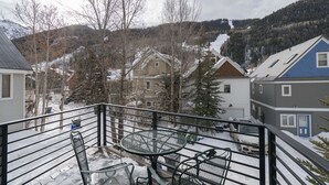 Varanda com mesa e cadeiras de metal, com vista para uma área residencial coberta de neve, com casas e árvores.