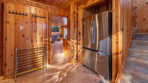 Interior em madeira com geladeira de aço inoxidável, uma estante de metal e lareira ao fundo.