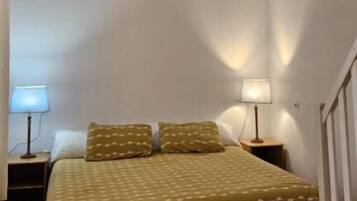 Quarto com cama, duas luminárias de apoio, edredom estampado e tapete escuro.