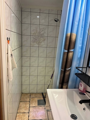 Casa de banho com chuveiro, paredes revestidas de azulejos, banheira e porta-toalhas.