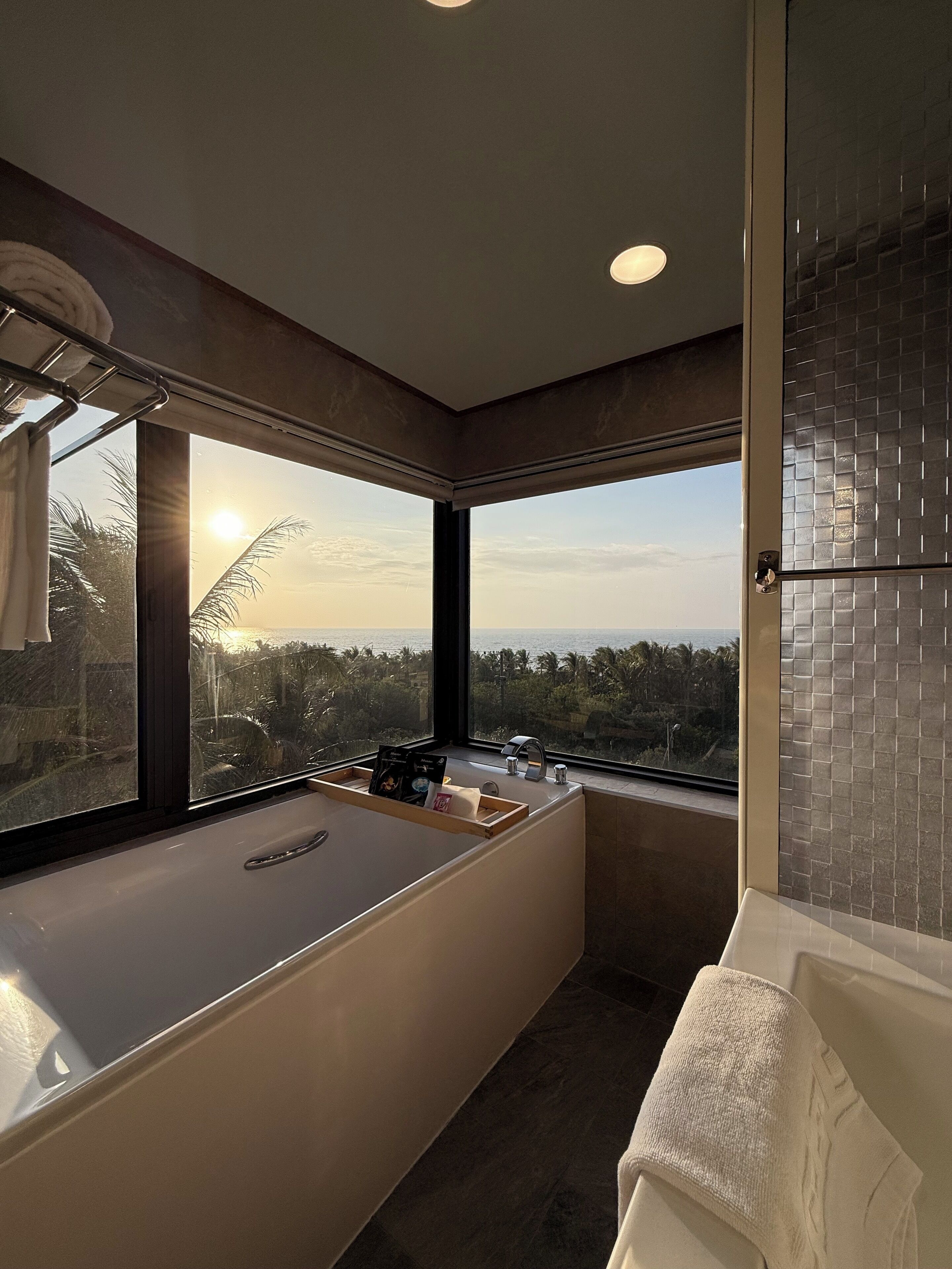 Um banheiro moderno com uma banheira grande, uma janela com vista para o mar e uma área de chuveiro revestida com azulejos.