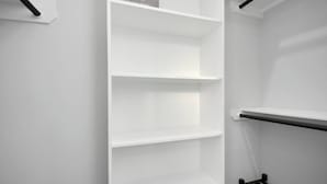 Interior branco com aquecedor embutido em toda a sala, uma estante de metal e um armário com prateleiras brancas.