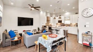 Um apartamento moderno com sala de estar, área de refeições, cozinha e uma televisão grande.