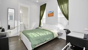 Quarto com cama, escrivaninha, cadeira, espelho e janela com cortinas.