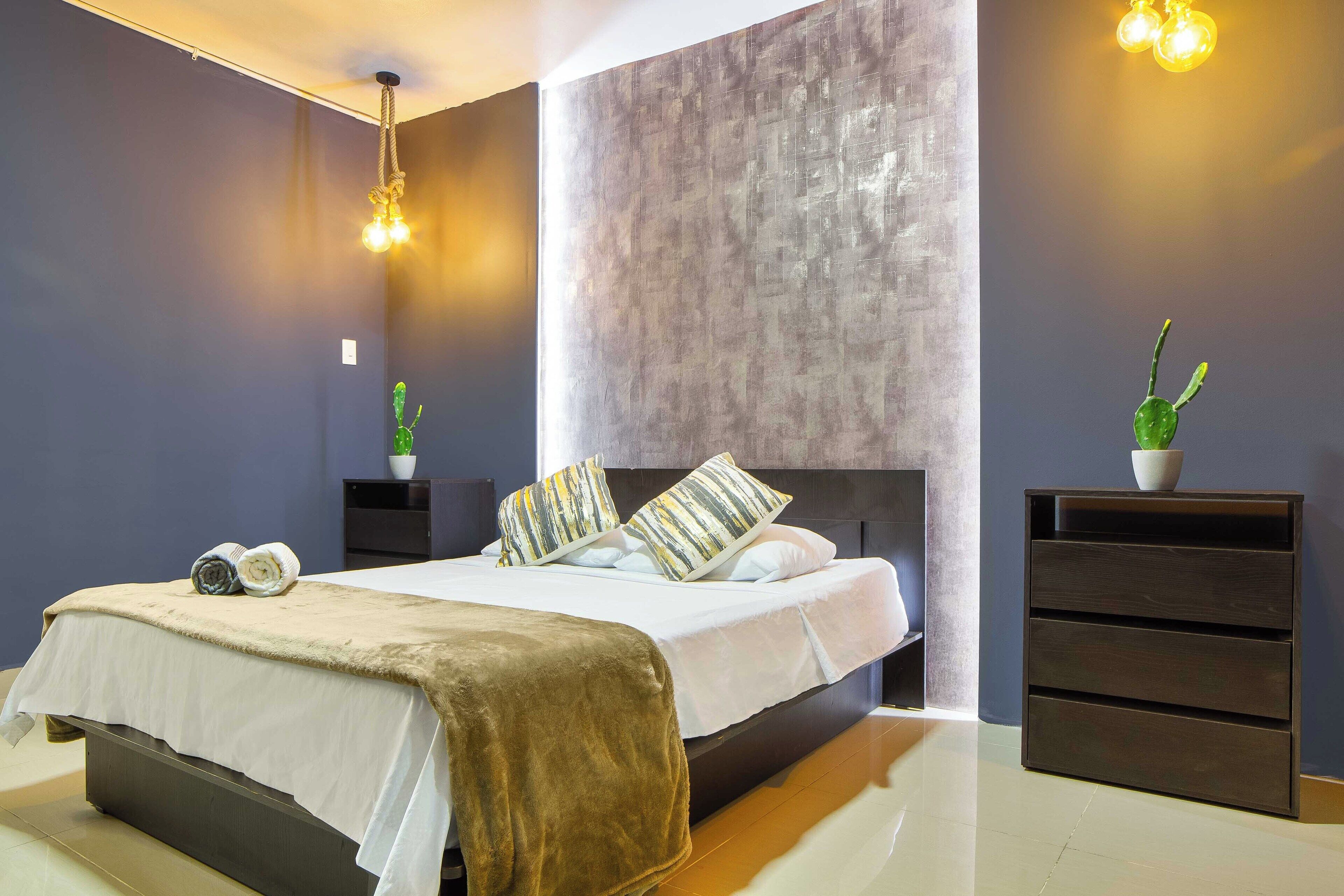 Um quarto moderno com cama, mesas de cabeceira, um criado-mudo e uma estante na parede.