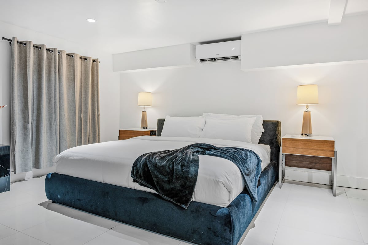 Quarto moderno com cama grande, mesas de cabeceira e ar condicionado.