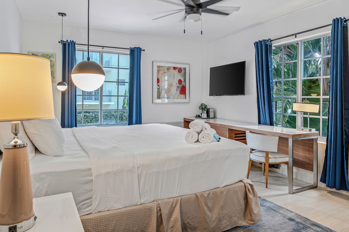 Quarto de hotel moderno com cama, escrivaninha e janelas amplas.