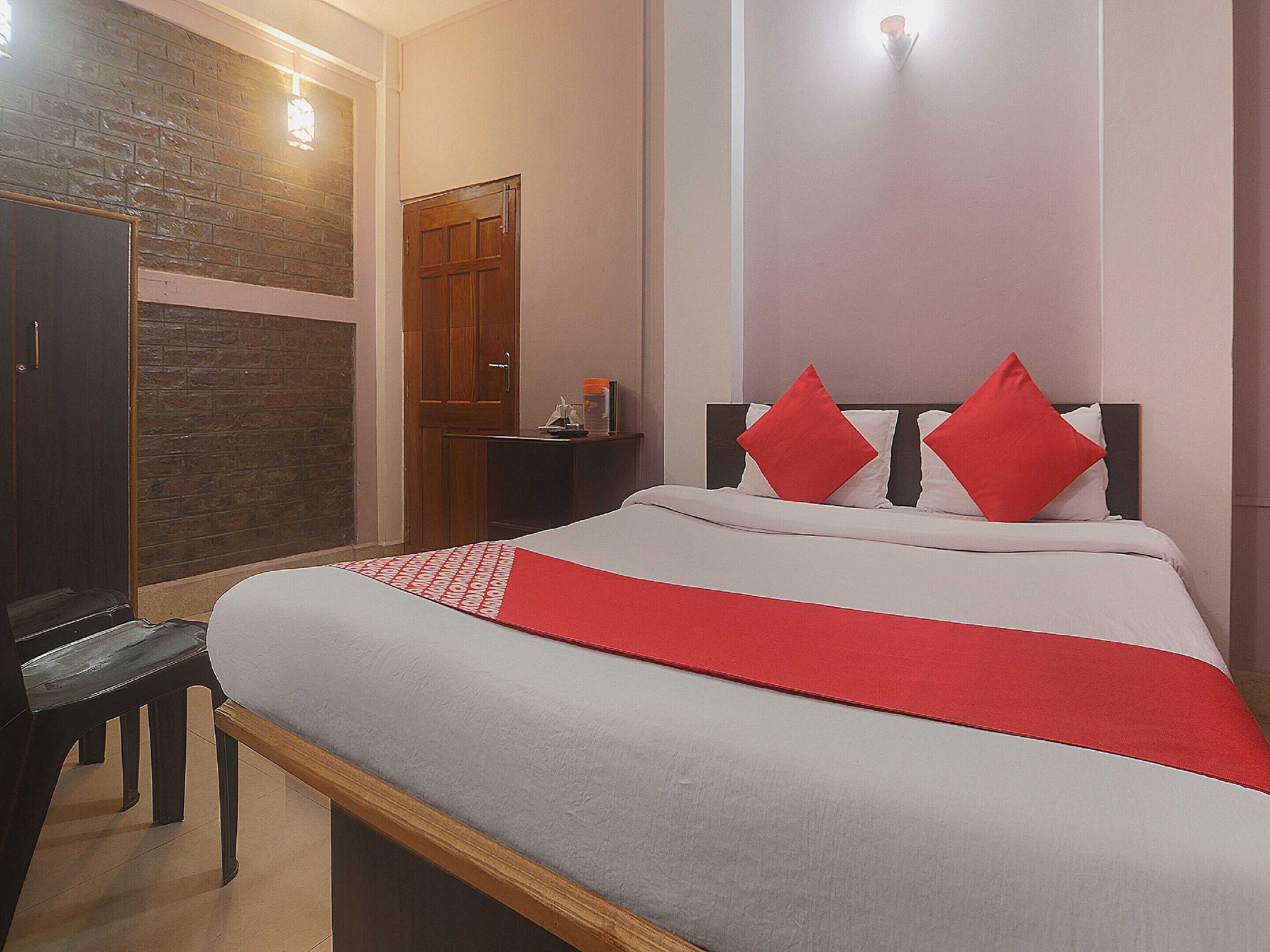 Quarto de hotel com uma cama, um banco de madeira, uma mesa de trabalho e um guarda-roupa.
