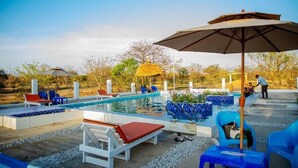 Área de piscina com espreguiçadeiras e guarda-sóis, rodeada por um jardim bem cuidado.