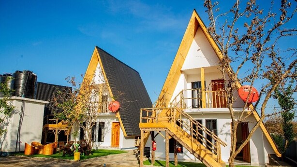 Um edifício moderno com telhado triangular, escadaria que leva a uma varanda e área de estar externa.
