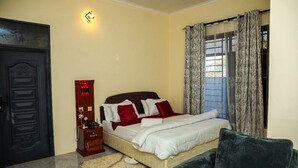 Quarto com cama, mesa de cabeceira, cômoda, abajur e janela com cortinas.