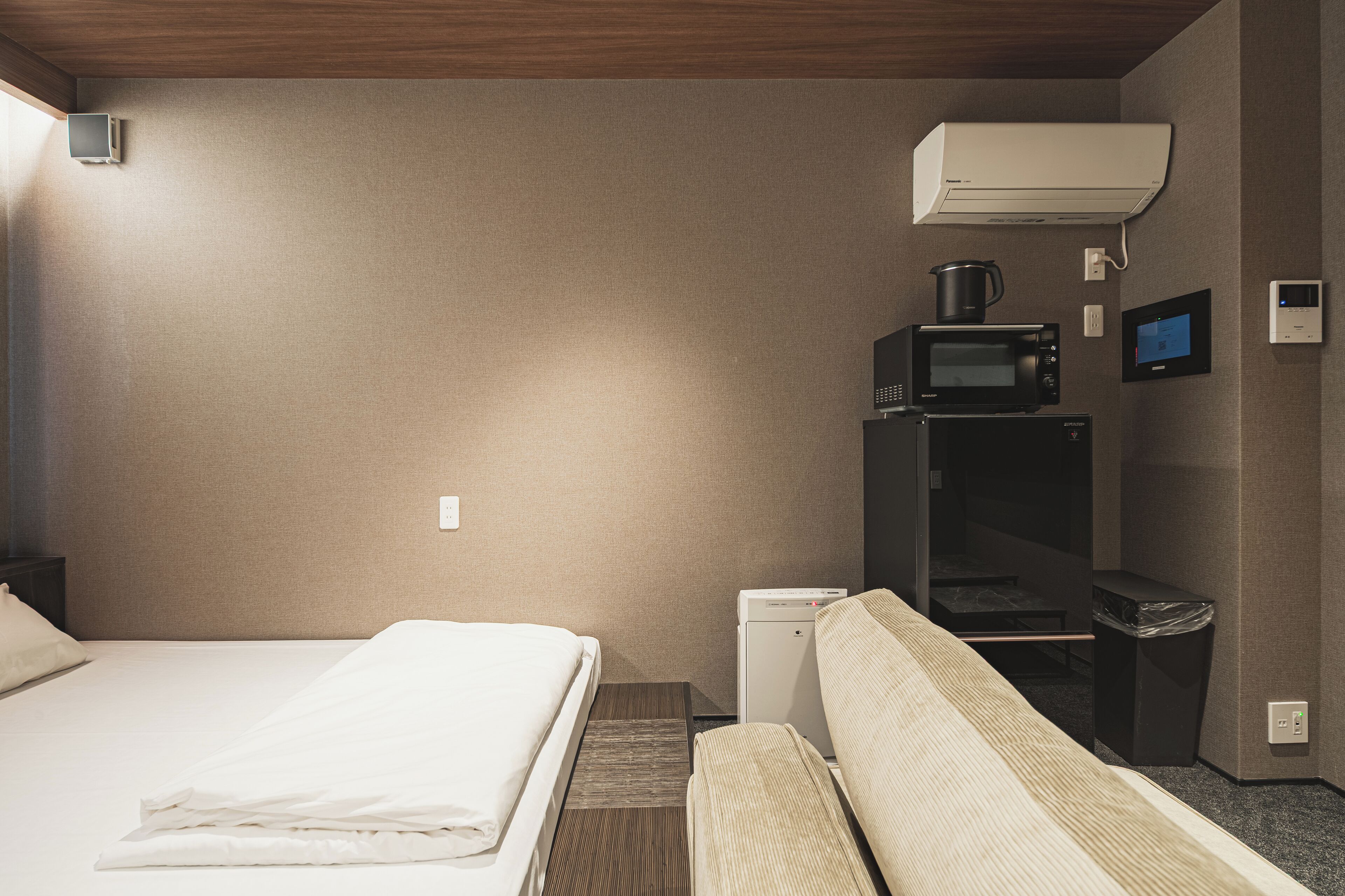 Quarto de hotel com cama, escrivaninha, micro-ondas, máquina de café e termostato na parede.