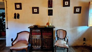 Quarto com duas cadeiras de madeira, uma mesa de madeira com um vaso e várias fotos emolduradas na parede.