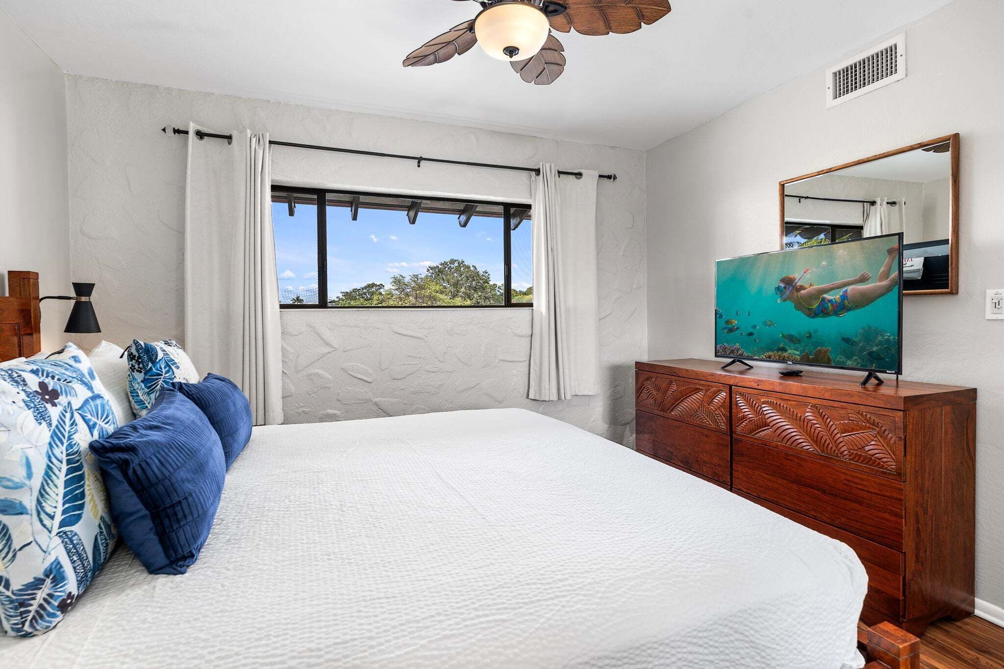 Quarto com uma cama grande, cômoda de madeira, televisão e janela com cortinas.