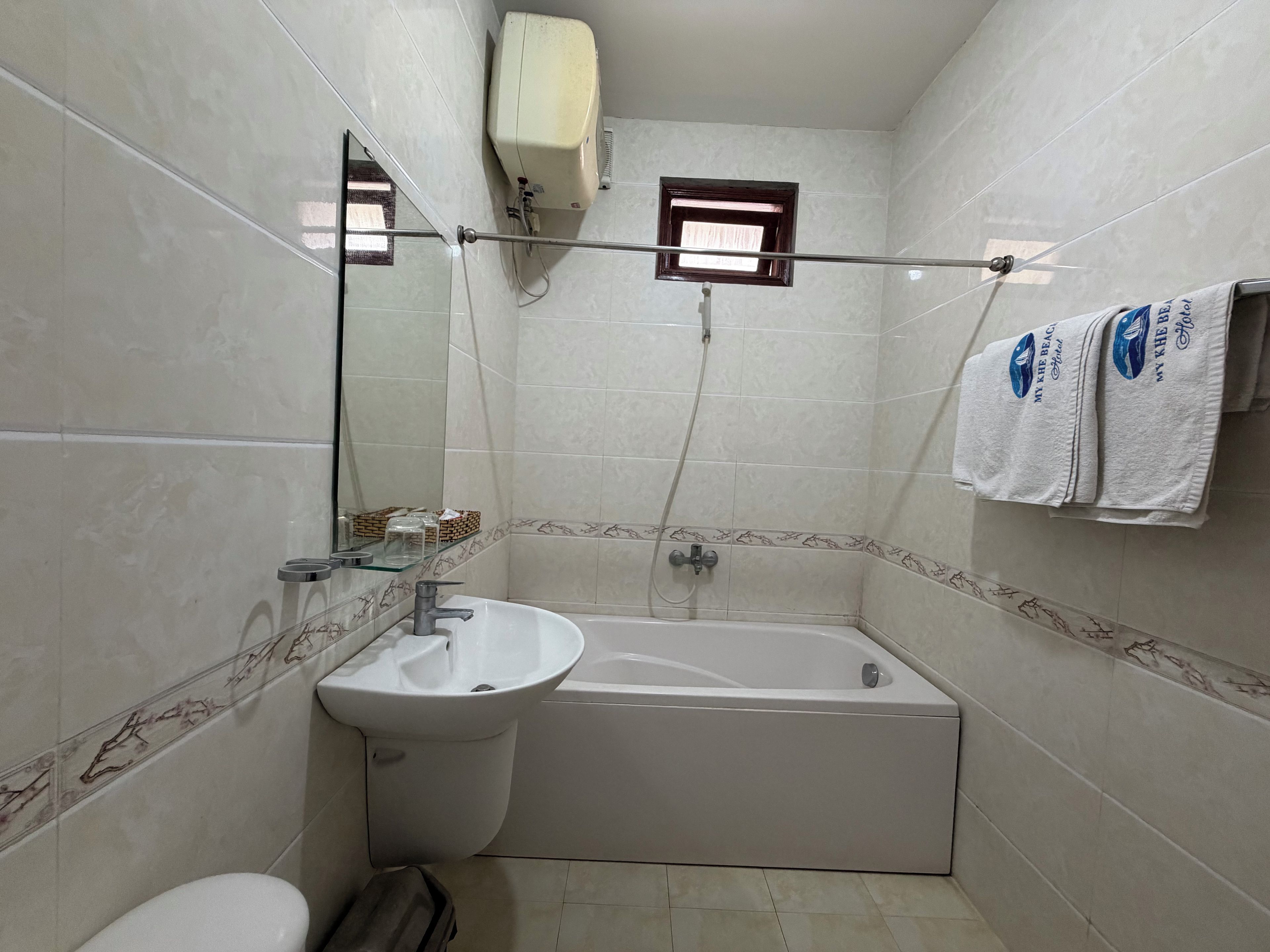 Casa de banho com lavatório, sanita e banheira. Inclui um porta-toalhas com toalhas, uma janela e um espelho.