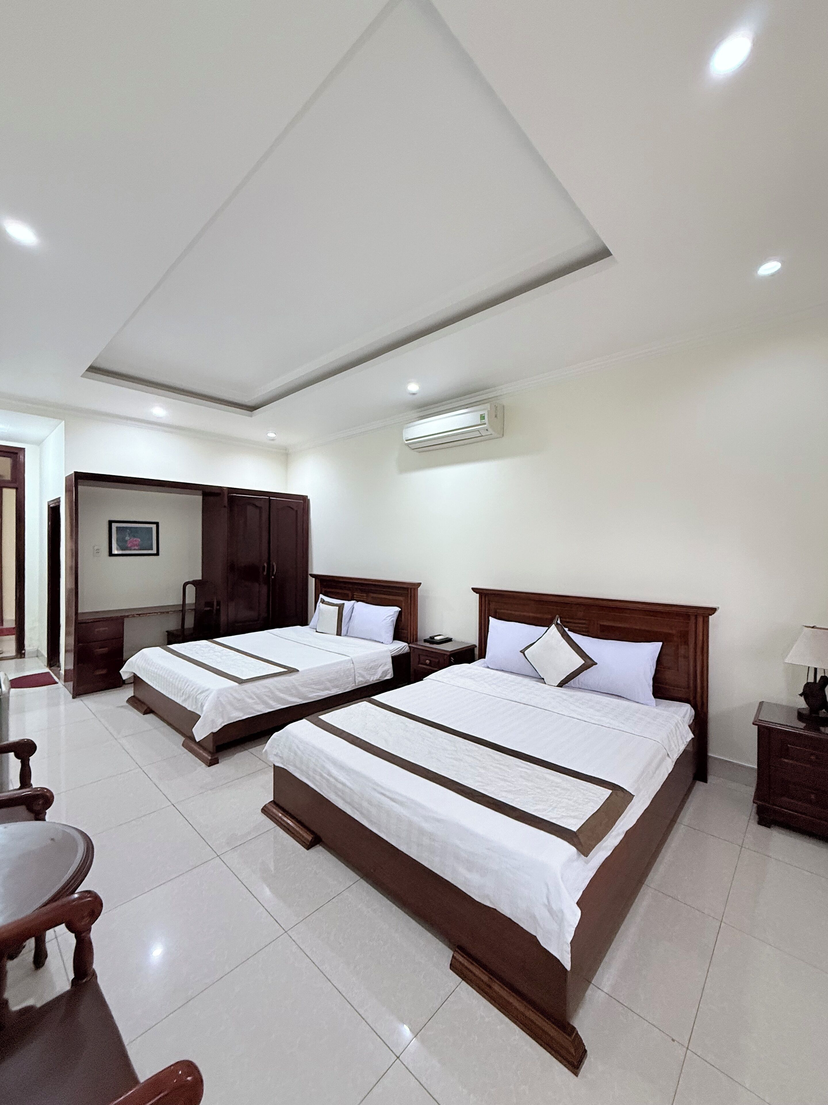 Quarto de hotel com duas camas, um guarda-roupa de madeira, uma escrivaninha e um ar condicionado.