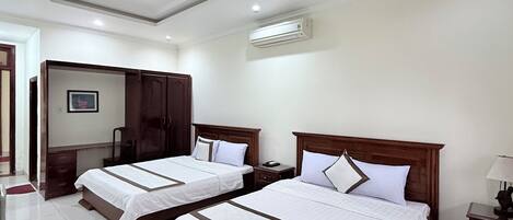 Quarto de hotel com duas camas, um guarda-roupa de madeira, uma escrivaninha e um ar condicionado.