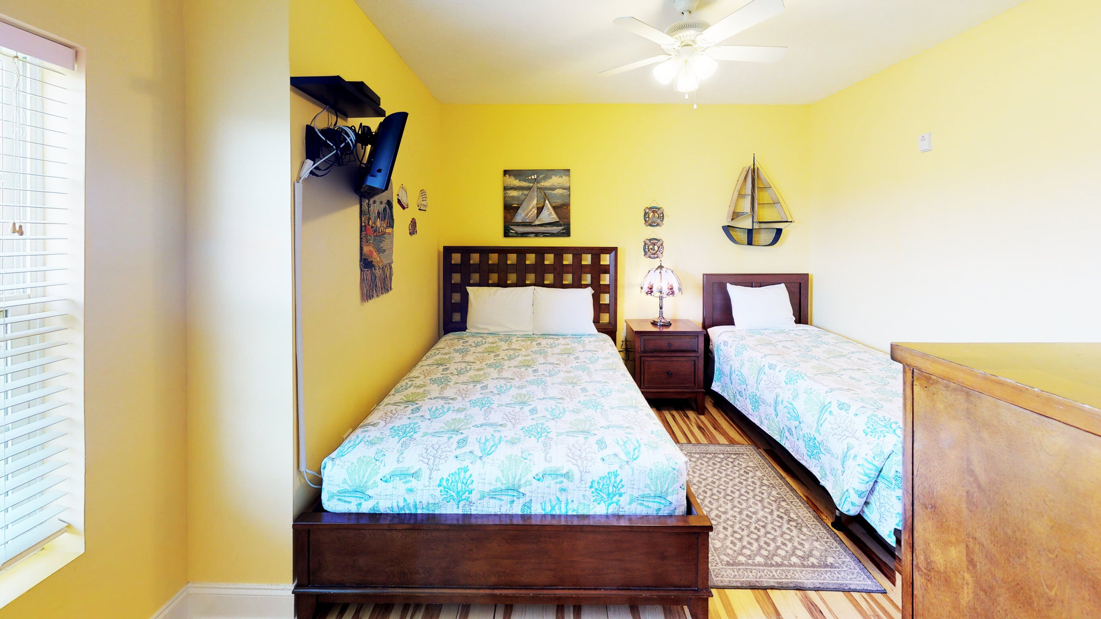 Quarto com duas camas, um ventilador de teto e janela com persianas.