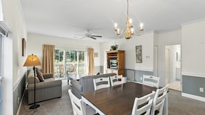 Uma sala de jantar com uma mesa de madeira, cadeiras brancas, um ventilador de teto e um candelabro.