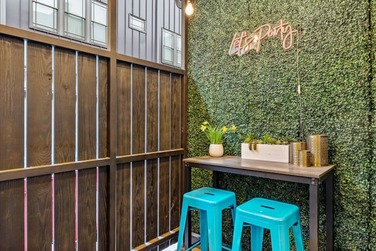 Um espaço interno aconchegante com uma divisória de madeira, uma parede verde com a placa 'Party' e dois banquinhos azuis.