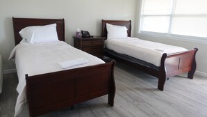 Quarto com duas camas de madeira, uma mesa de cabeceira e janela com persianas.