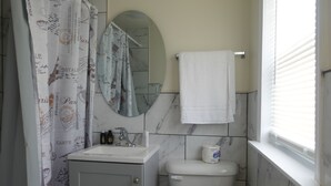 Casa de banho com lavatório branco, espelho, sanita e cortina de chuveiro com padrões de texto.