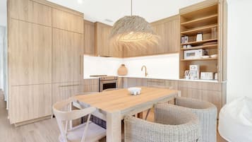 Cozinha moderna com armários de madeira, ilha central, cadeiras de vime e luminária pendente.