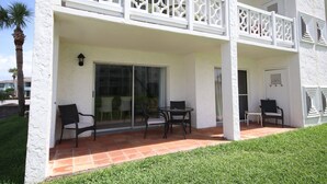 Alpendre coberto com mesa e cadeiras, guarda-corpo branco e uma palmeira.