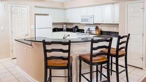 Cozinha moderna com armários brancos, uma ilha central com banquetas, micro-ondas e cafeteira.