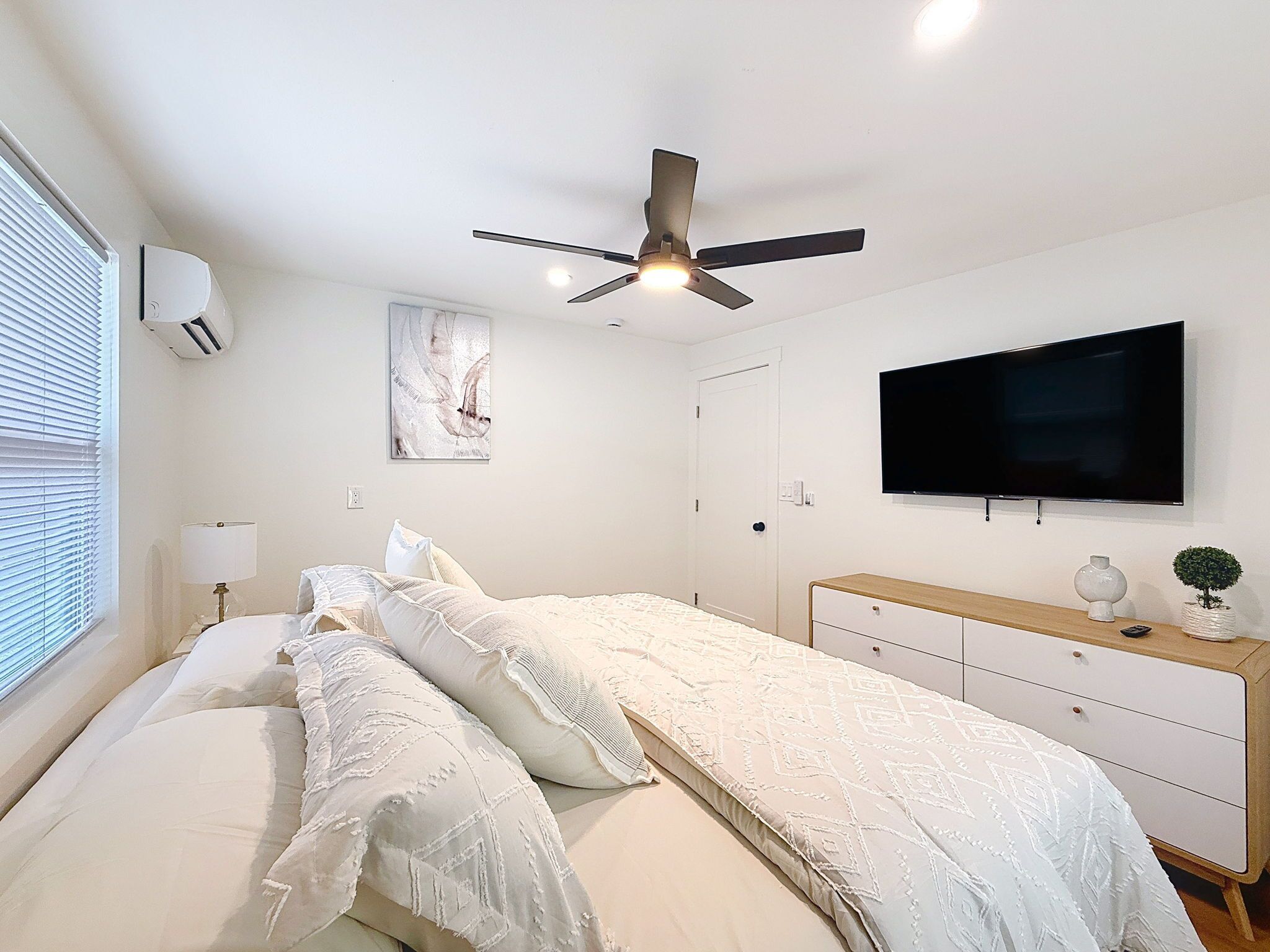 Quarto com cama, ventoinha no teto, televisão, cômoda e janela com persianas.