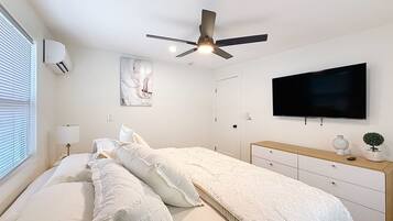 Quarto com cama, ventoinha no teto, televisão, cômoda e janela com persianas.