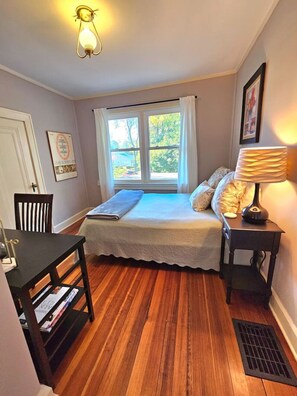 Quarto com uma cama, escrivaninha, cadeira, janela e luminária.