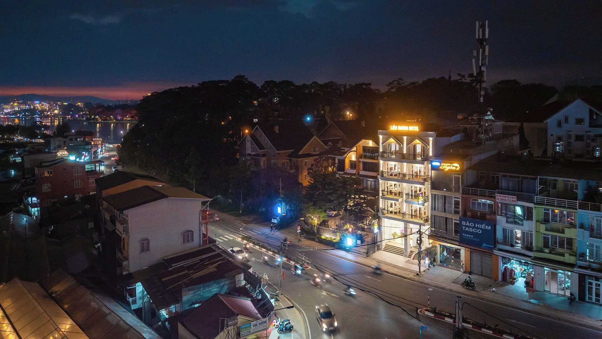 Um hotel de vários andares com sinalização iluminada, uma rua com veículos e edifícios ao redor.
