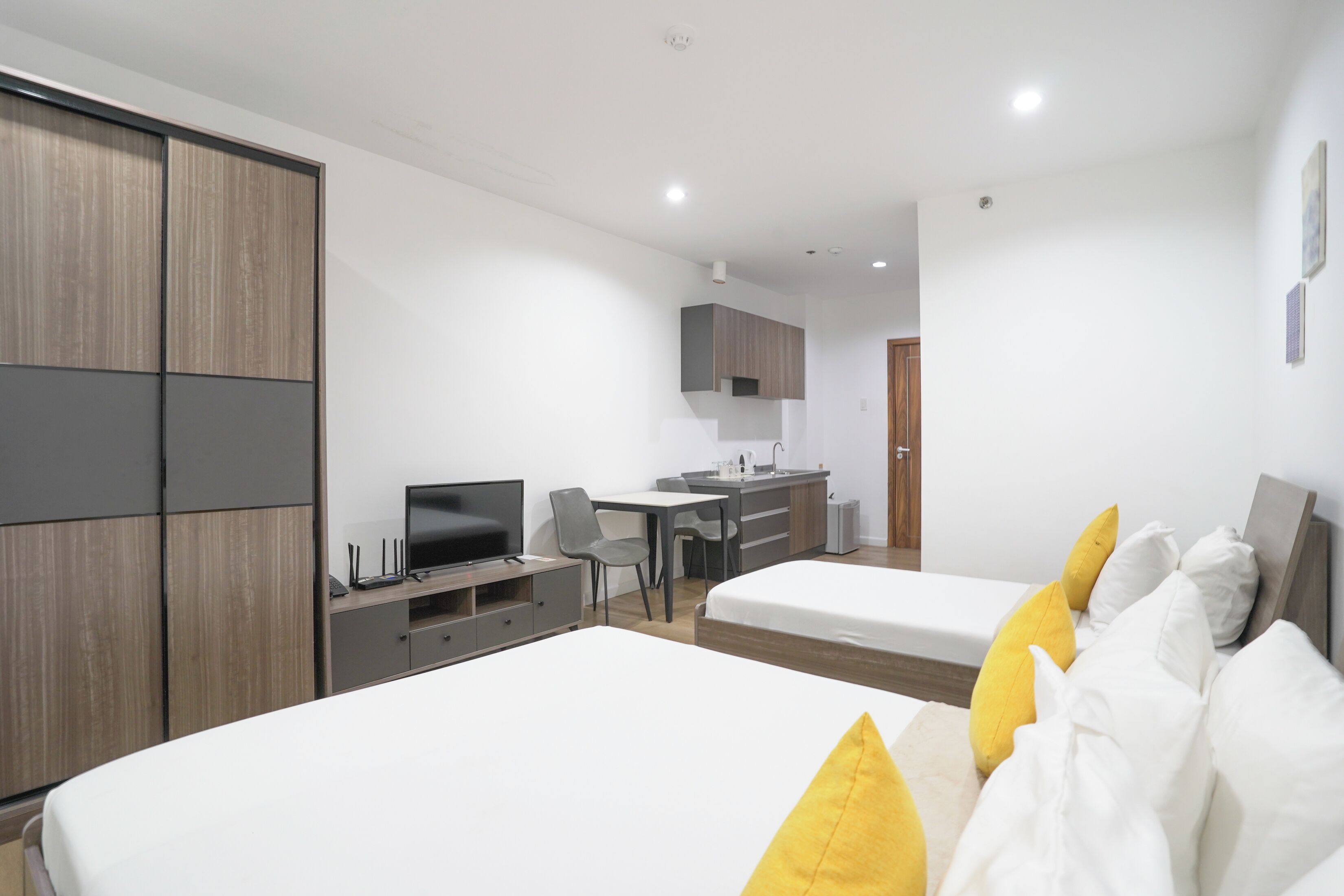 Quarto de hotel moderno com cama, escrivaninha, televisão e cozinha compacta.