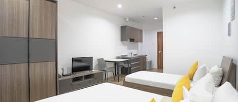 Quarto de hotel moderno com cama, escrivaninha, televisão e cozinha compacta.