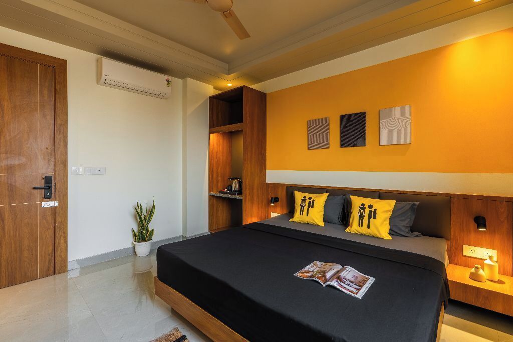 Quarto de hotel moderno com uma cama grande, cabeceira de madeira e uma parede de destaque em amarelo vibrante.