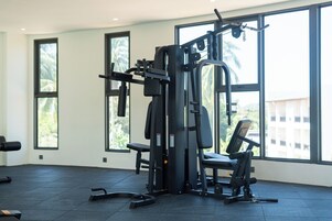 Academia com equipamentos de exercícios, grandes janelas e um banco.