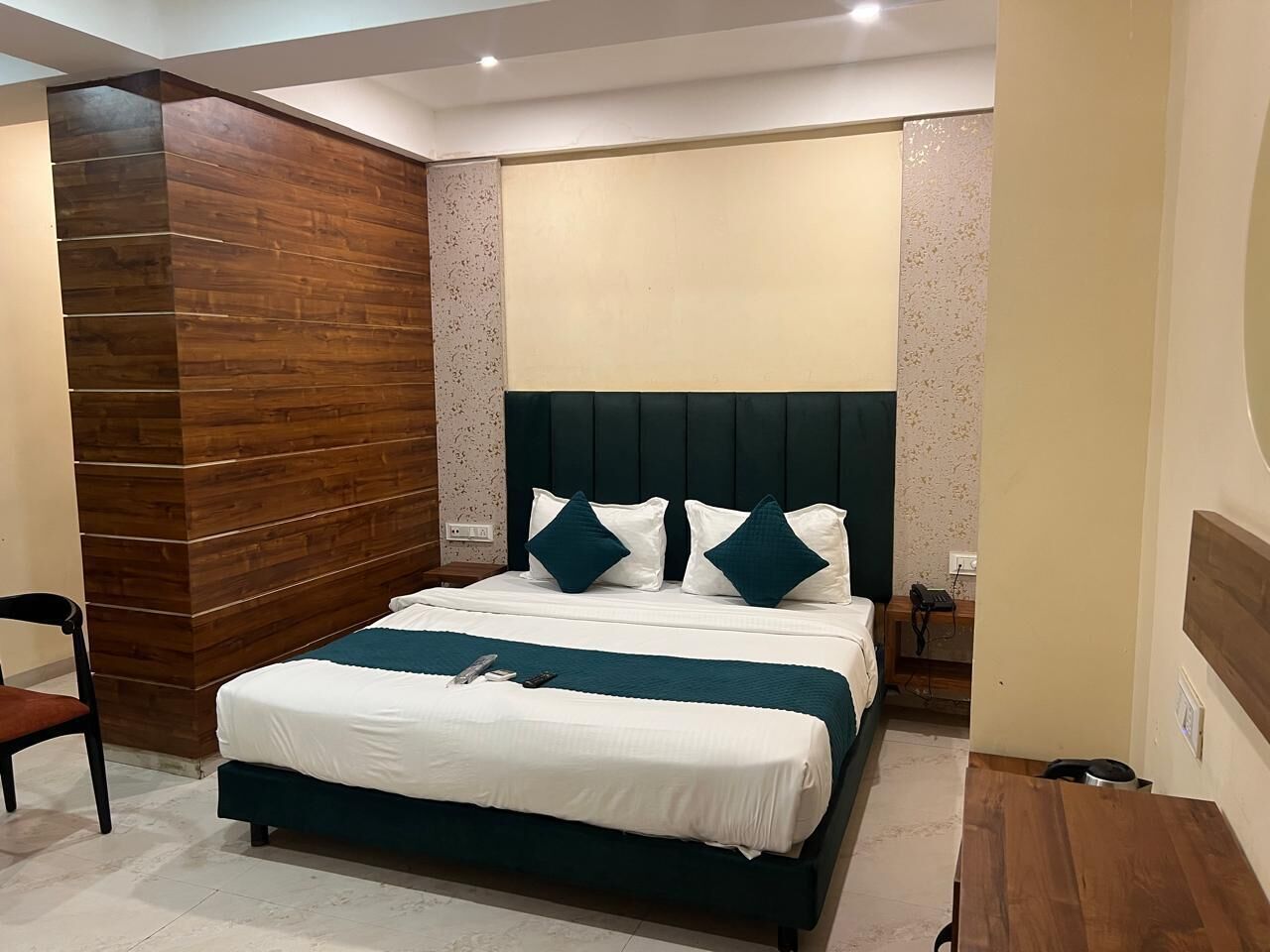 Quarto de hotel moderno com uma cama grande, cabeceira escura e uma parede de destaque em madeira.
