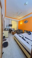 Quarto de hotel com cama, sofá, escrivaninha com computador e ventoinha no teto.