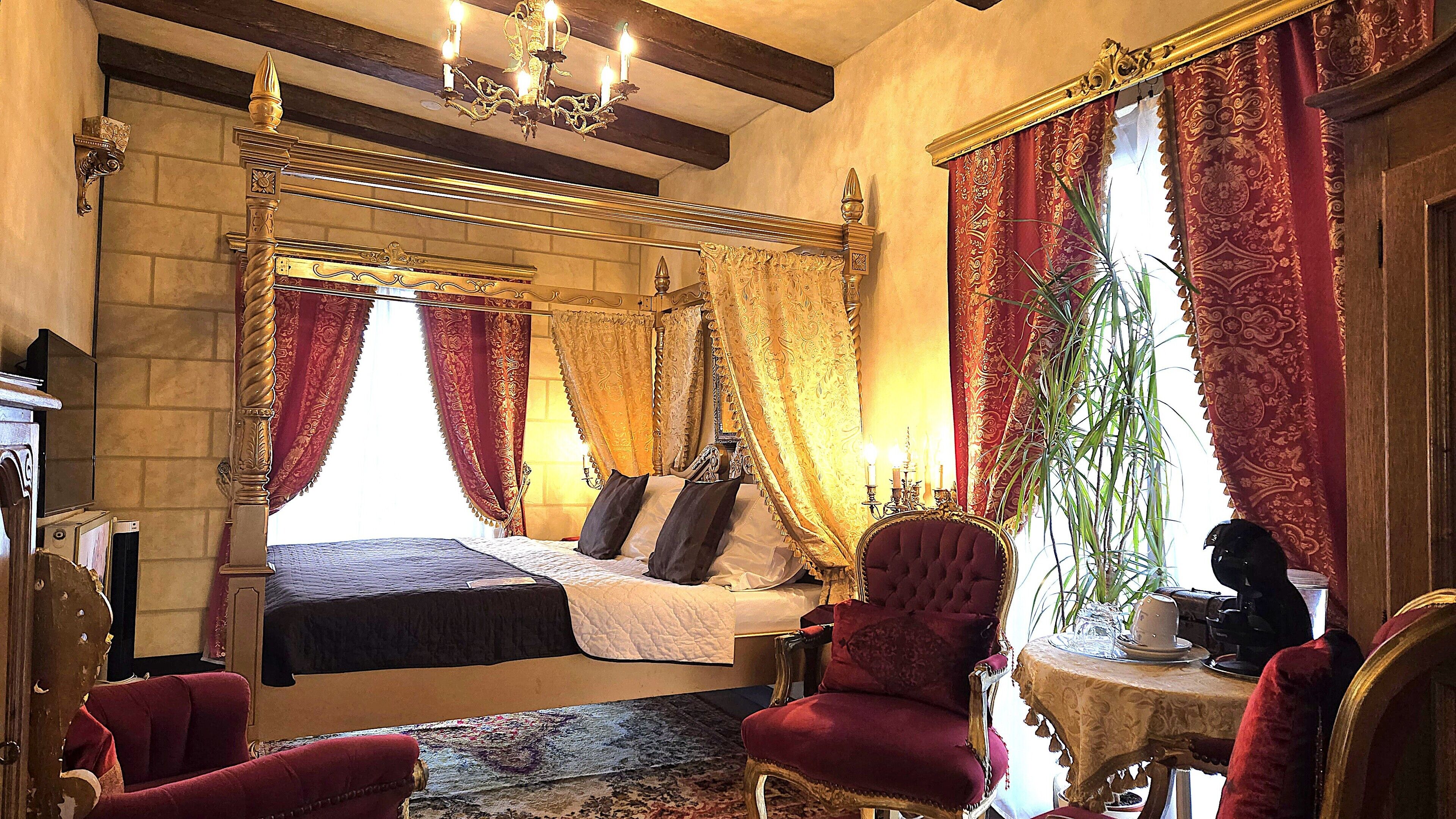 Um quarto luxuoso com cama de dossel, cortinas ornamentadas e um candelabro.