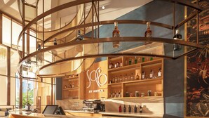 Uma área de bar com balcão curvo, prateleiras com garrafas e um letreiro com a inscrição 'SOHO BY ANYLA'.