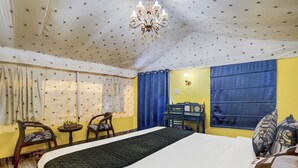 Quarto de hotel com uma cama, duas cadeiras, uma mesinha, uma escrivaninha e um candelabro.