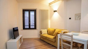 Uma sala de estar moderna com sofá, televisão sobre um móvel, mesa de jantar com cadeiras e janela com persianas.