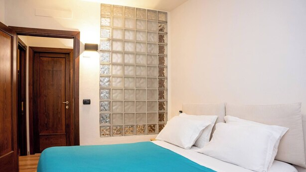 Quarto com porta de madeira, cama com roupa de cama branca e janela de vidro fosco.