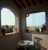 Um quarto com uma mesa, cadeiras, uma janela com vista para o campo e uma gaiola de pássaros pendurada.